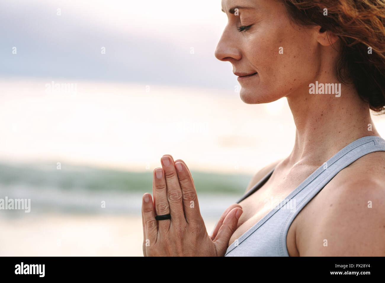 Side view of a fitness woman standing at the beach meditating with ...