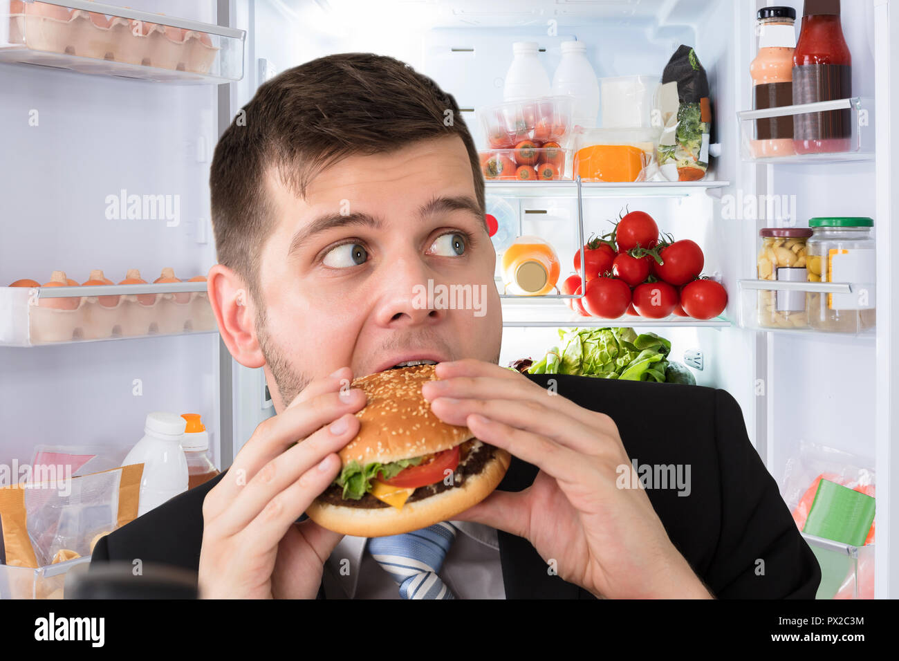 Young Businessman Eating Burger In Front Of An Open Refrigerator Stock ...