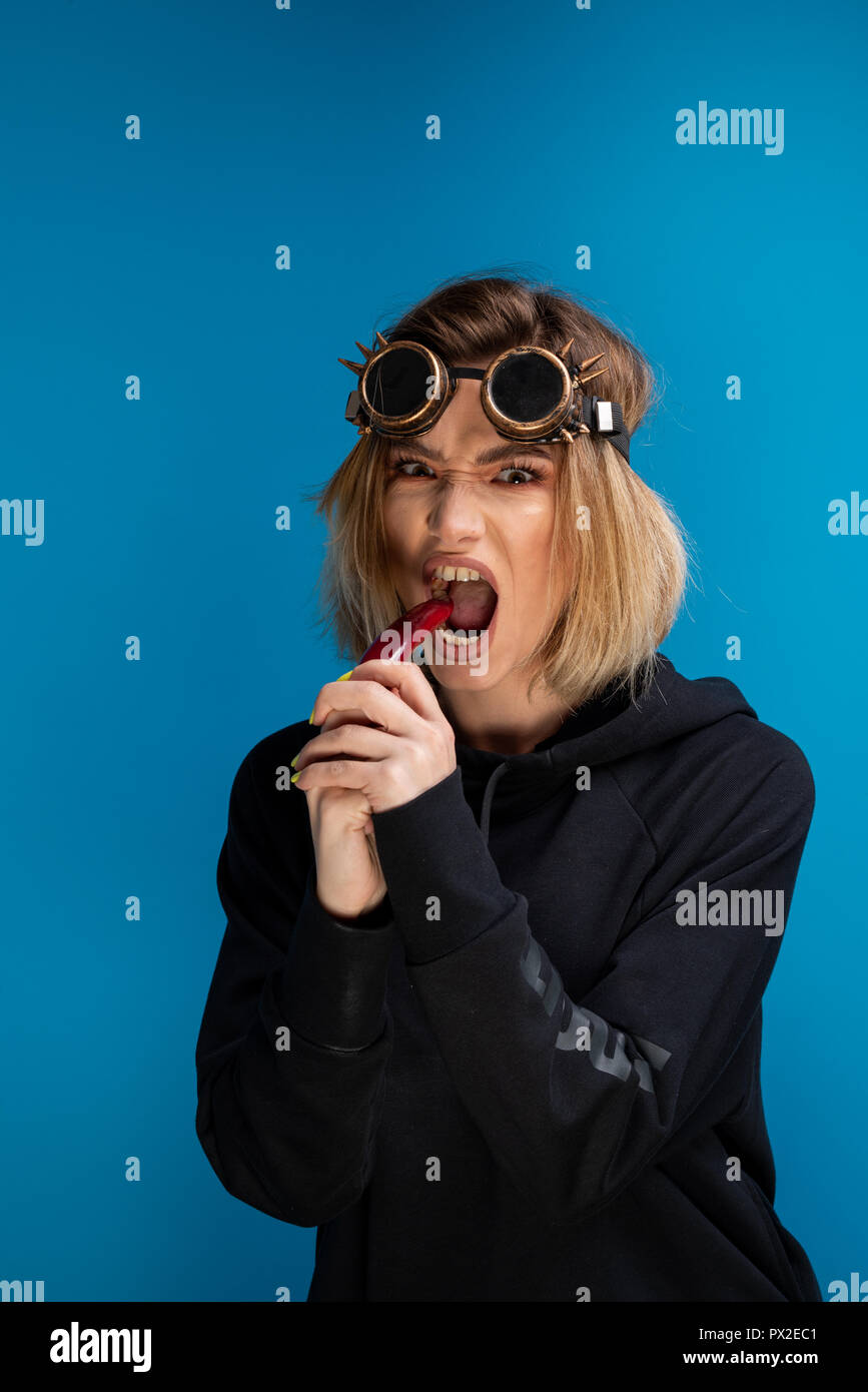 Angry steam punk girl with glasses biting a dark red chilli pepper with ...