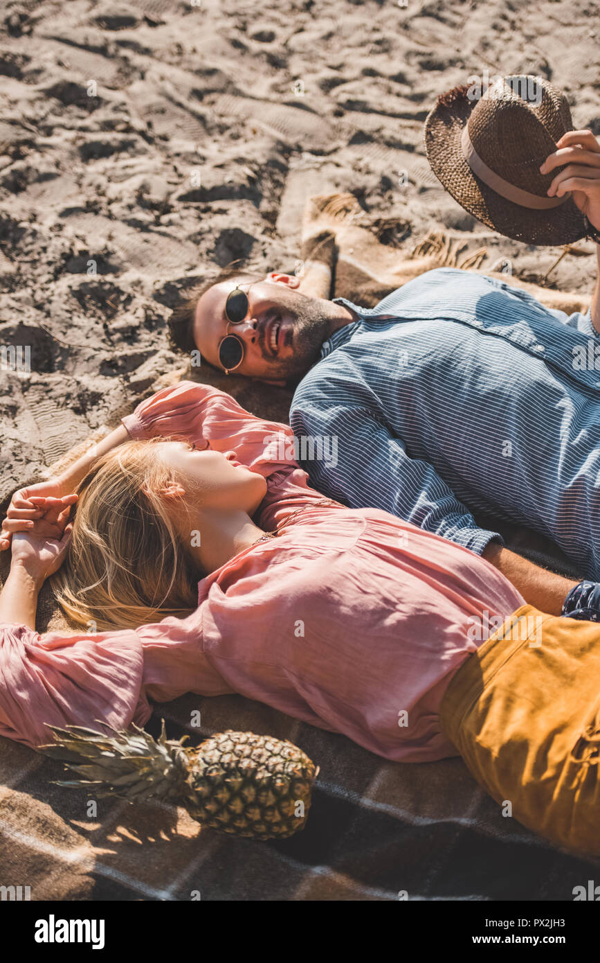 hippie couple looking at each other and relaxing on blanket on sand ...
