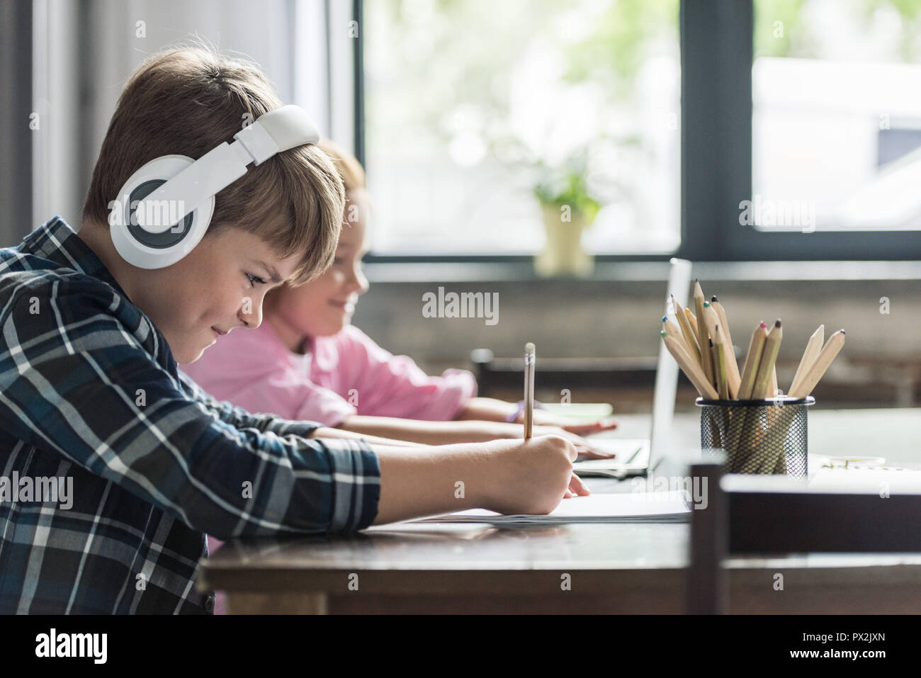 side view of smiling little schoolboy drawing with color pencils while ...