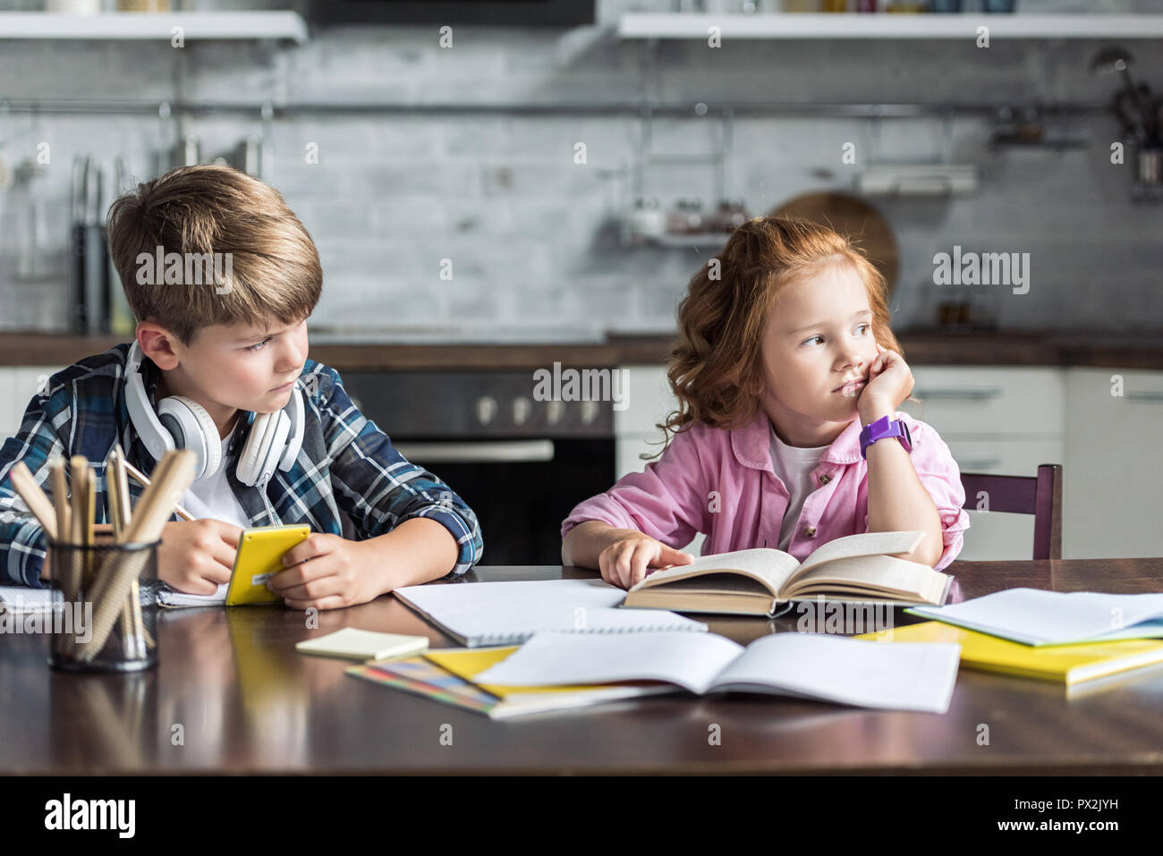 sad little brother and sister doing homework after quarrel at kitchen ...
