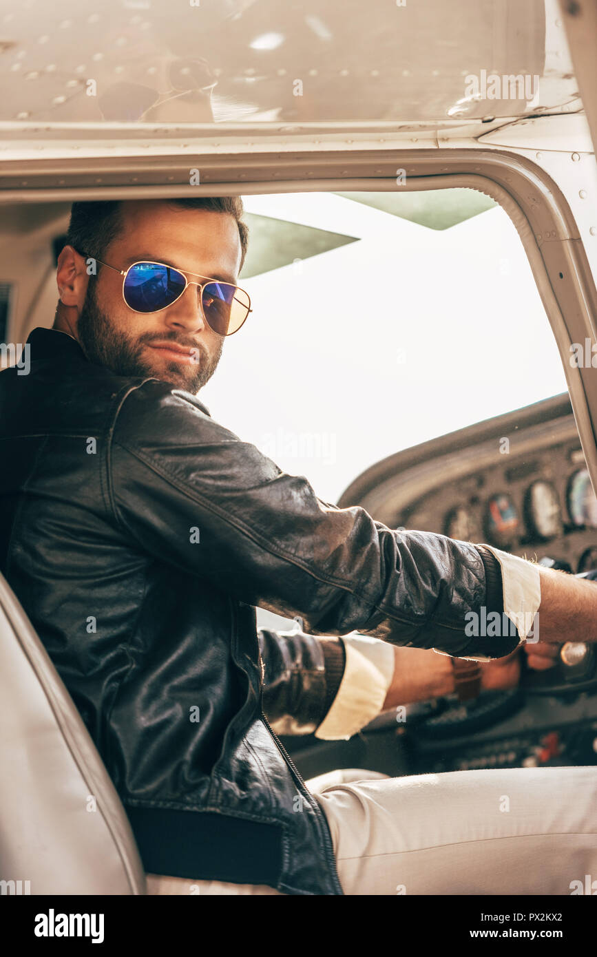 stylish male pilot in leather jacket and sunglasses sitting in airplane ...