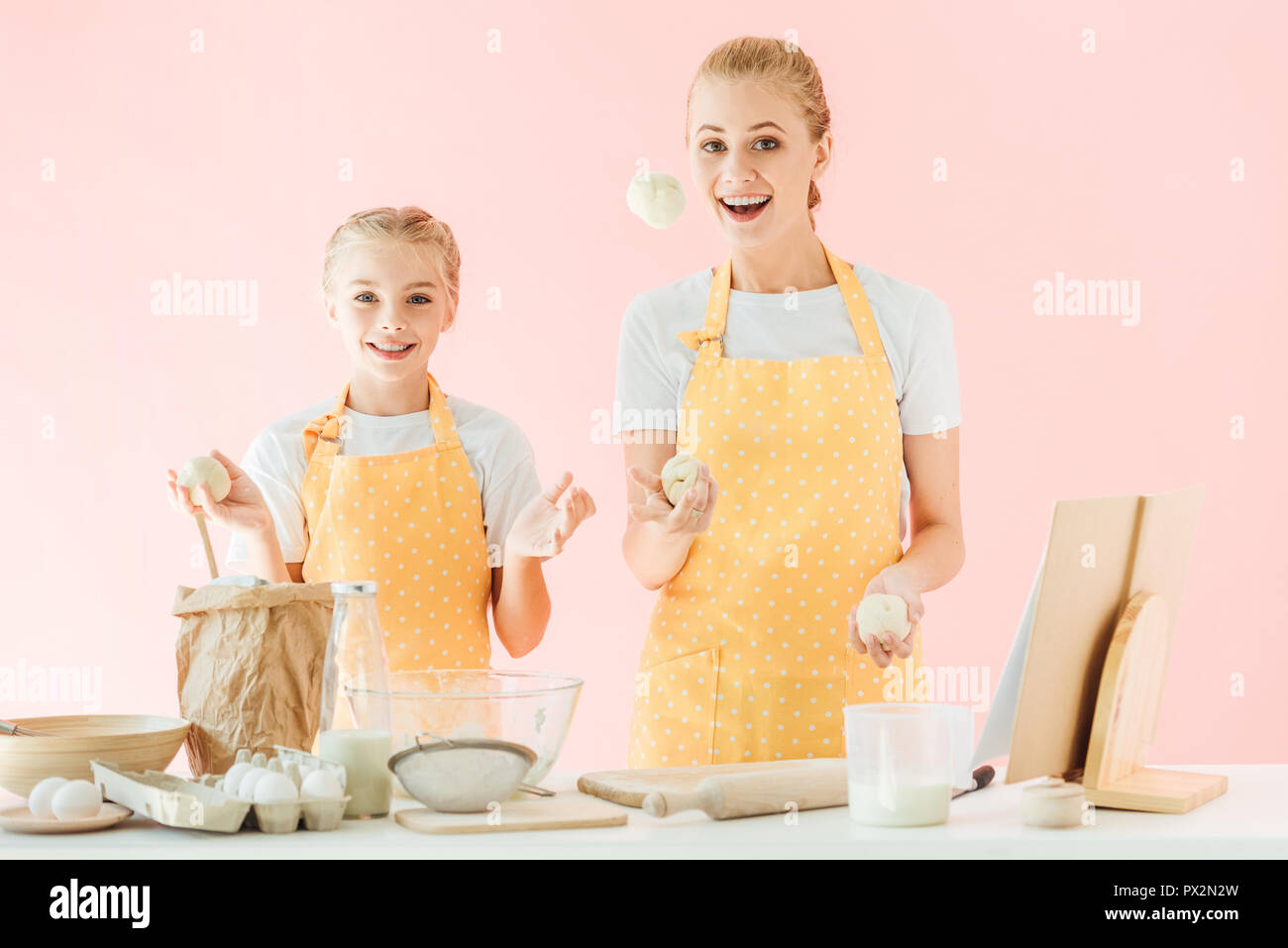 happy mother and daughter juggling with dough pieces while cooking ...