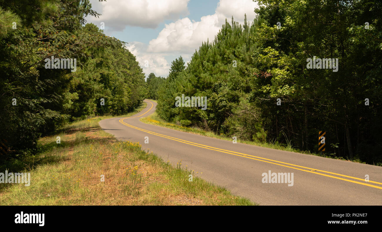 A two lane asphalt road winds up the hill and around the bend in ...