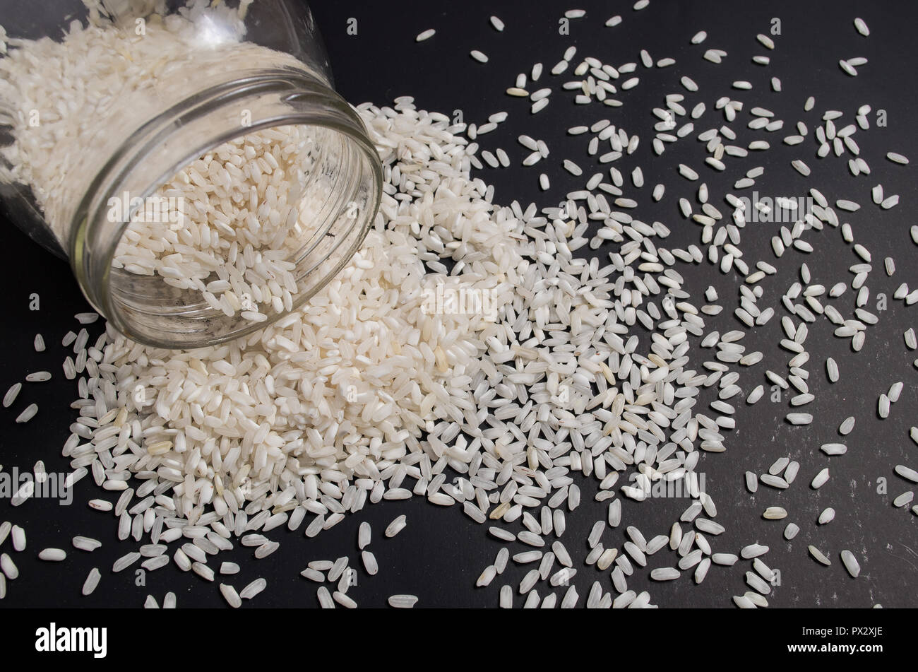 Rice scattered on an isolated black background, transparent glass jar ...