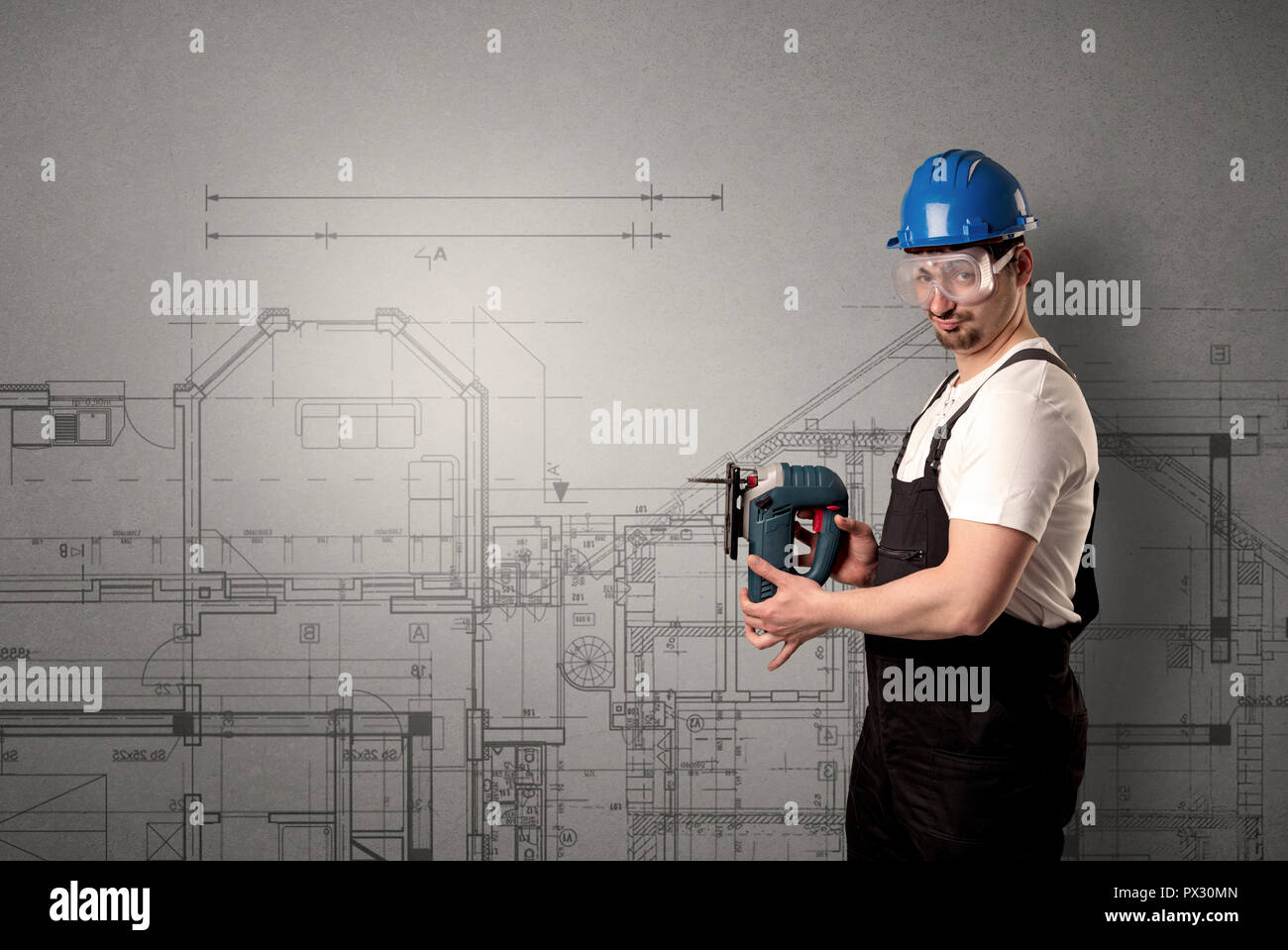Worker standing with tool in his hand in front of technical drawings ...
