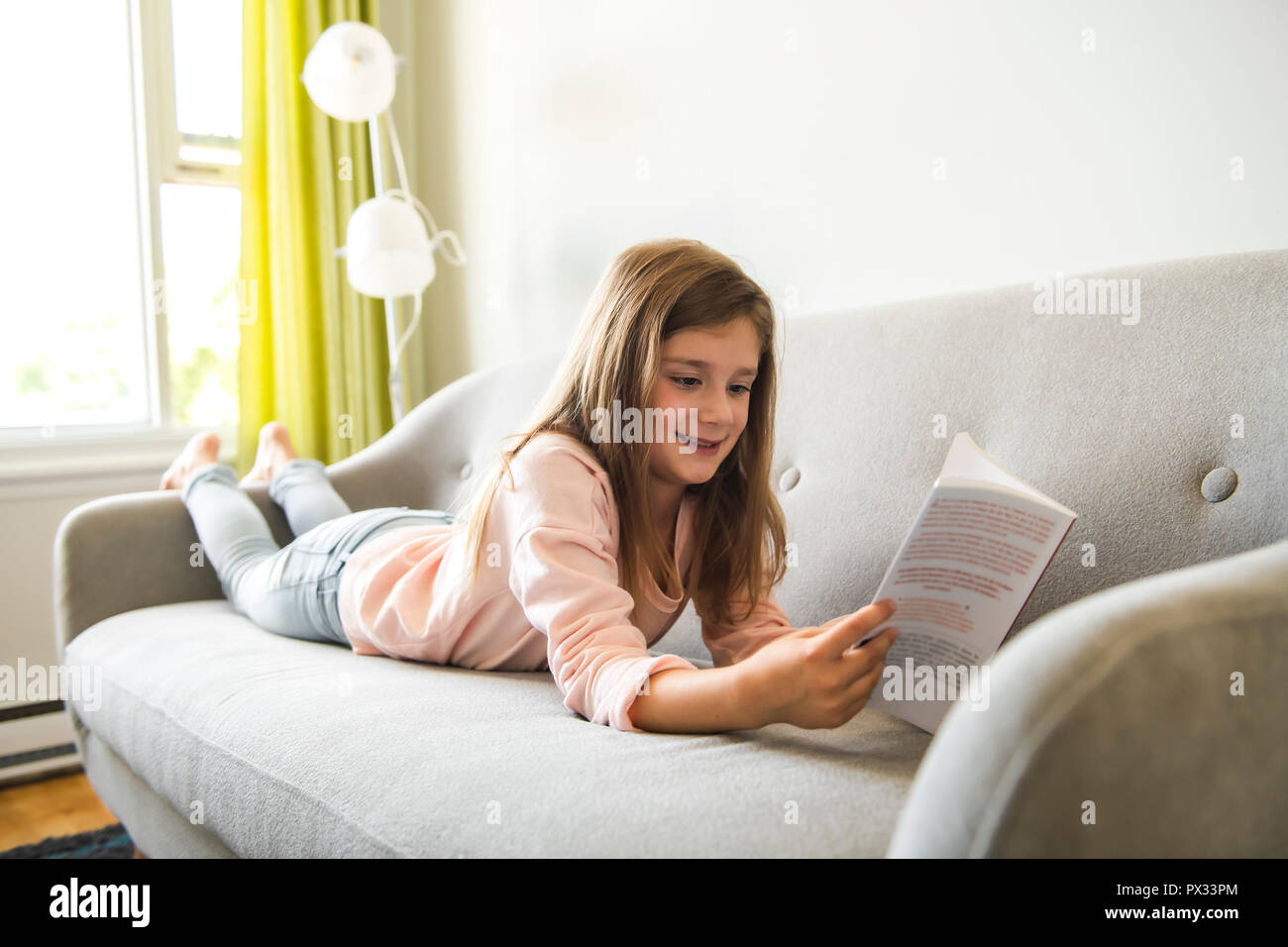 Girl Reading Book On Sofa In Living Room At Home Stock Photo - Alamy