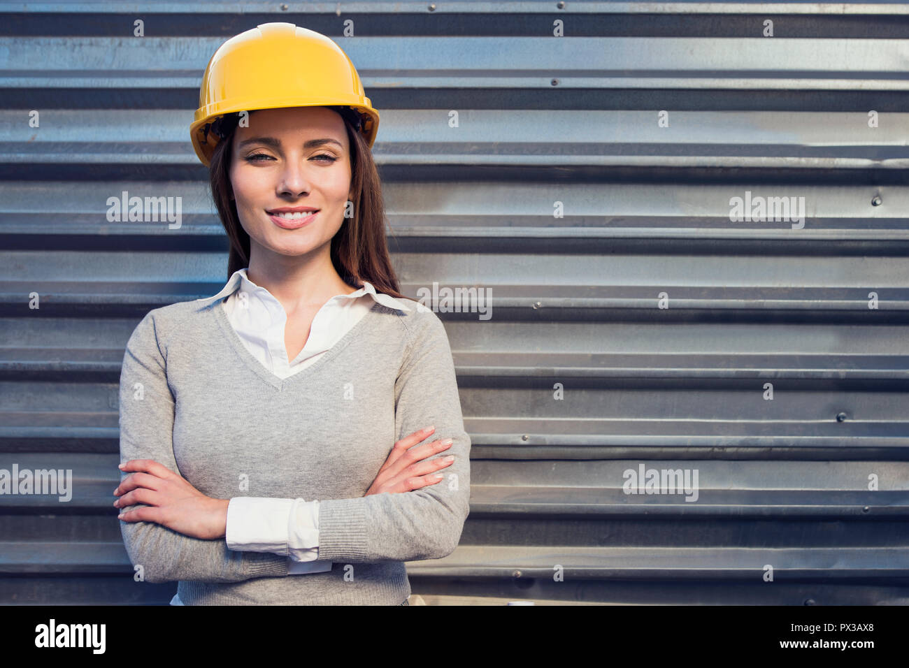 beautiful woman engineer is standing in front of an industrial wall ...