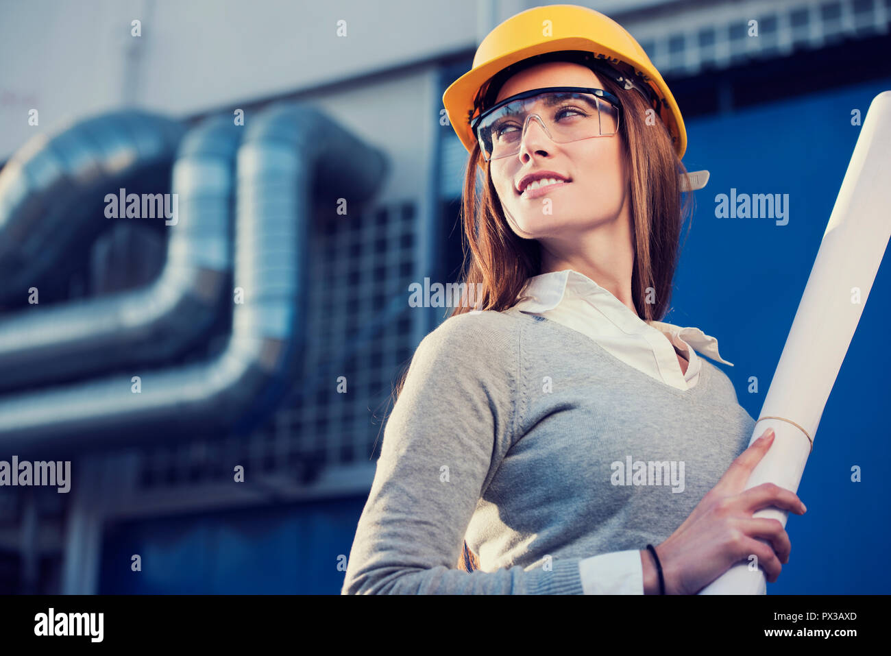 beautiful woman engineer is standing in front of an industrial pipes ...