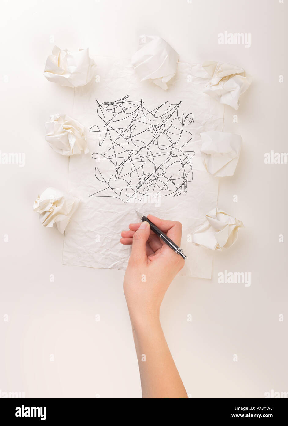 Female hand next to a few crumpled paper balls drawing random scribbles ...