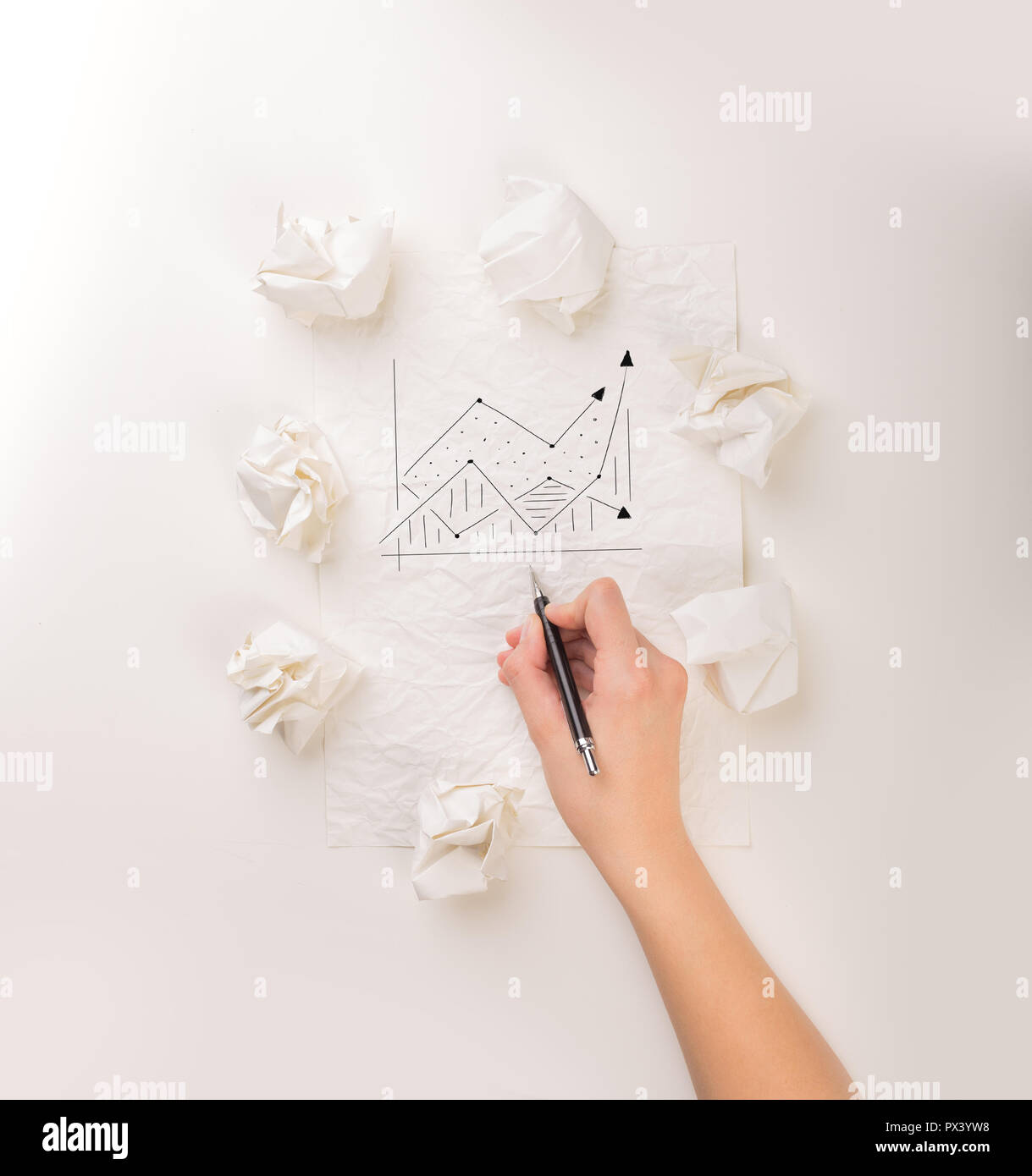 Female hand next to a few crumpled paper balls drawing a progress chart ...