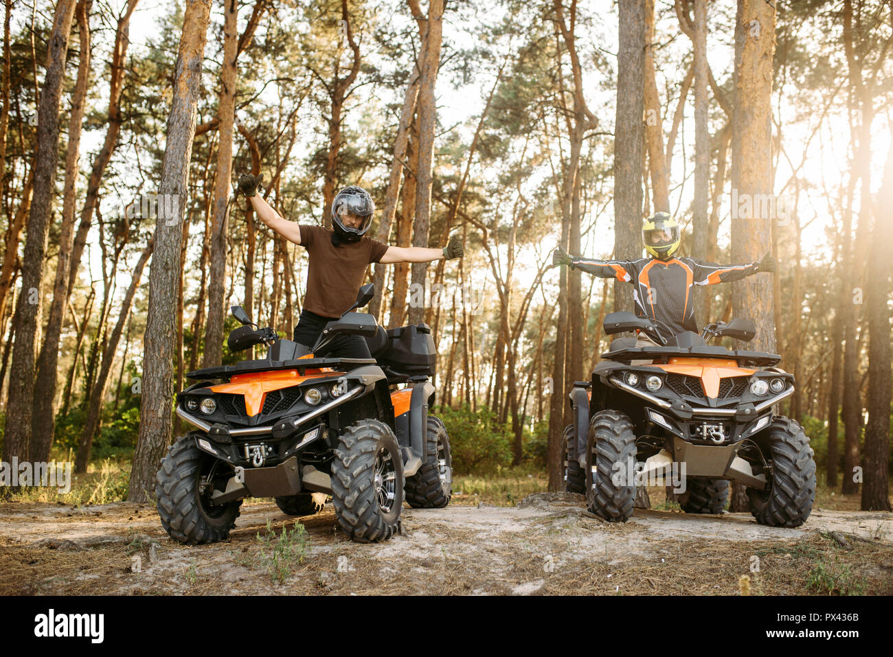 Two atv riders in helmets raise their hands up Stock Photo - Alamy