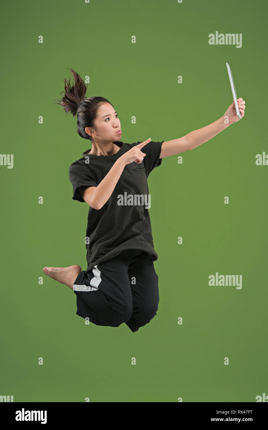 Gadget in modern life. Jump of young woman over green studio background ...