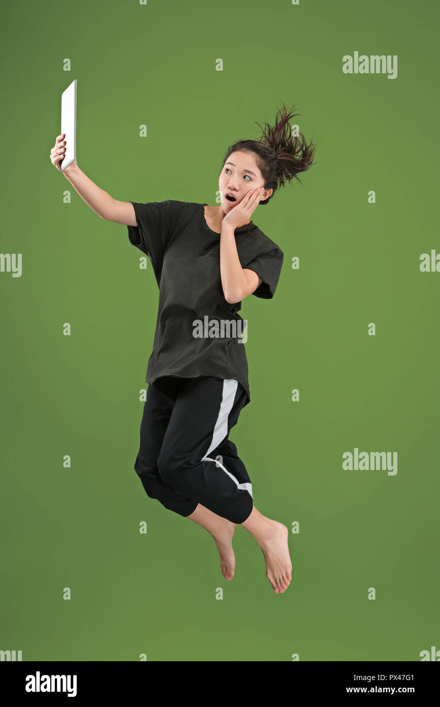 Gadget in modern life. Jump of young woman over green studio background ...