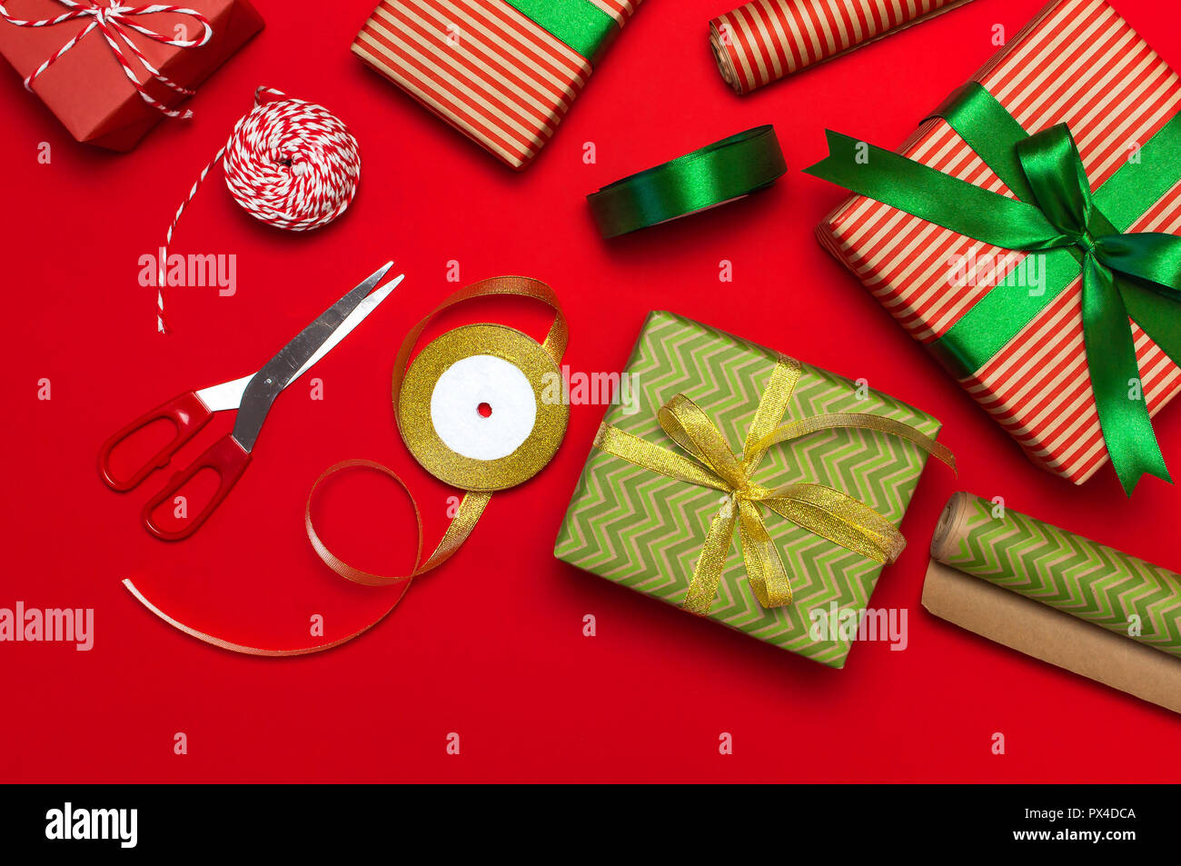 Gift boxes, packing paper, scissors, ribbon on red background. Festive ...