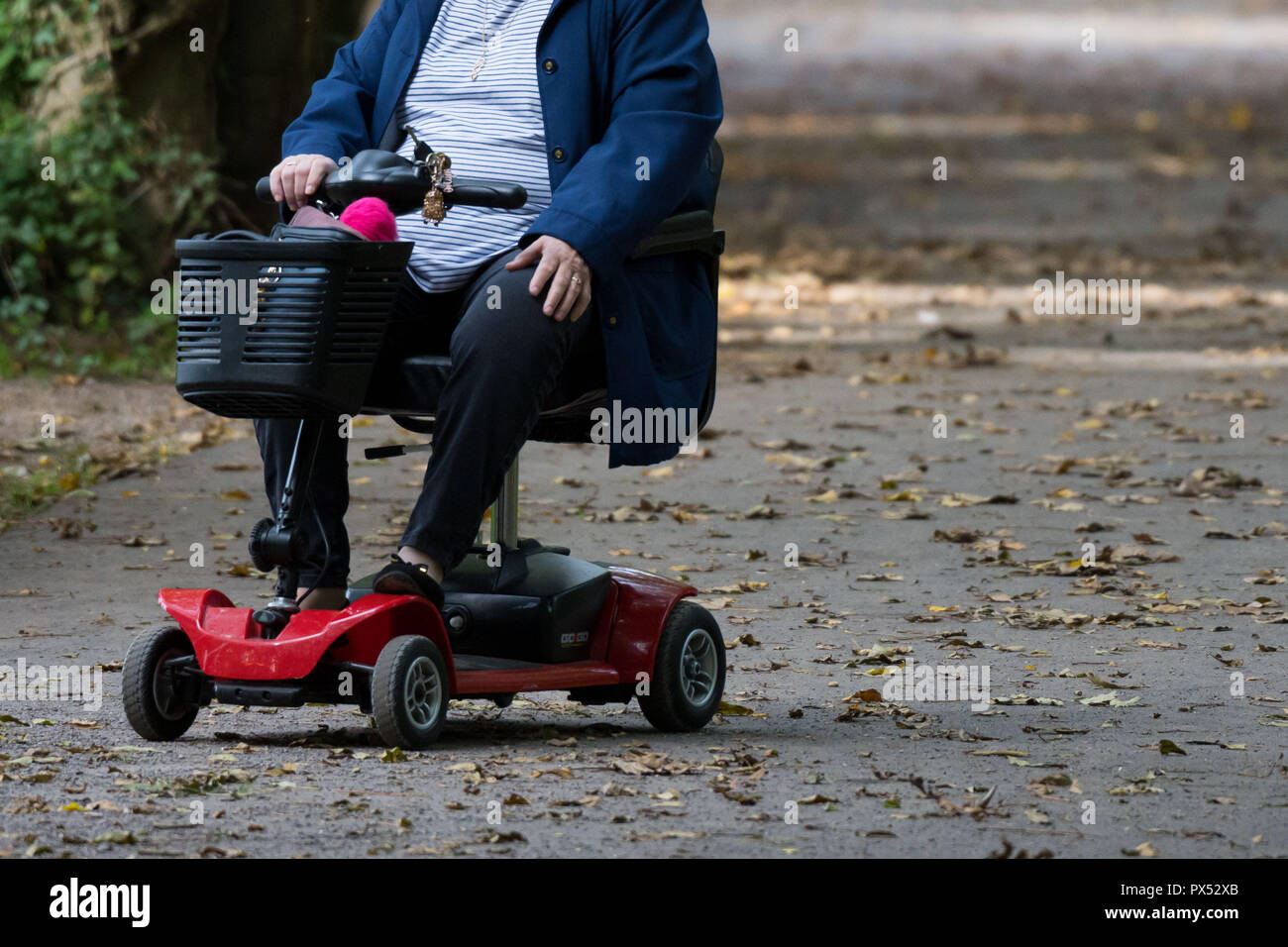 An elderly woman drives a mobility scooter on a pathway in the UK Stock ...
