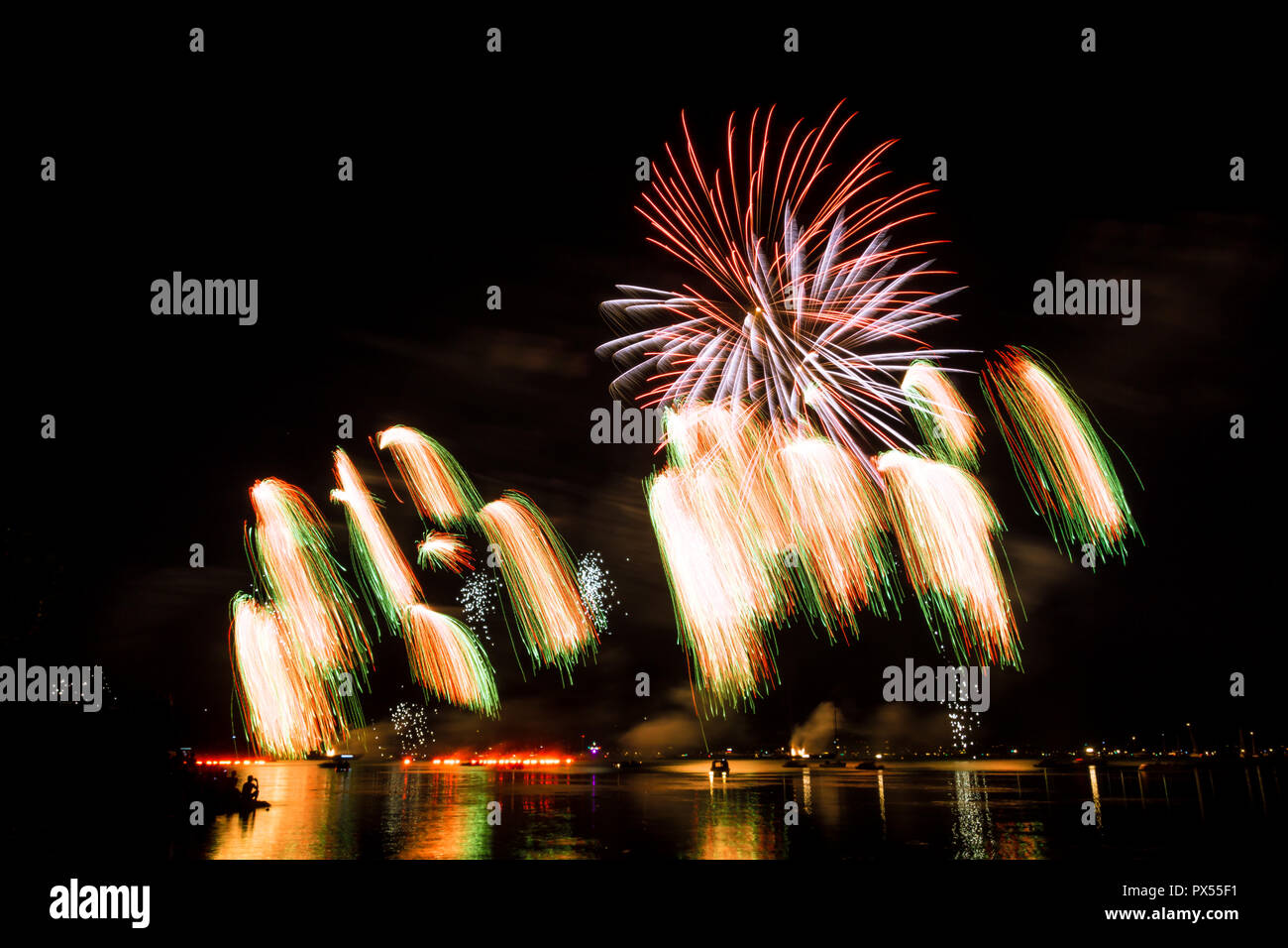 Huge colorful fireworks explosions and fire rain in the night at a lake ...