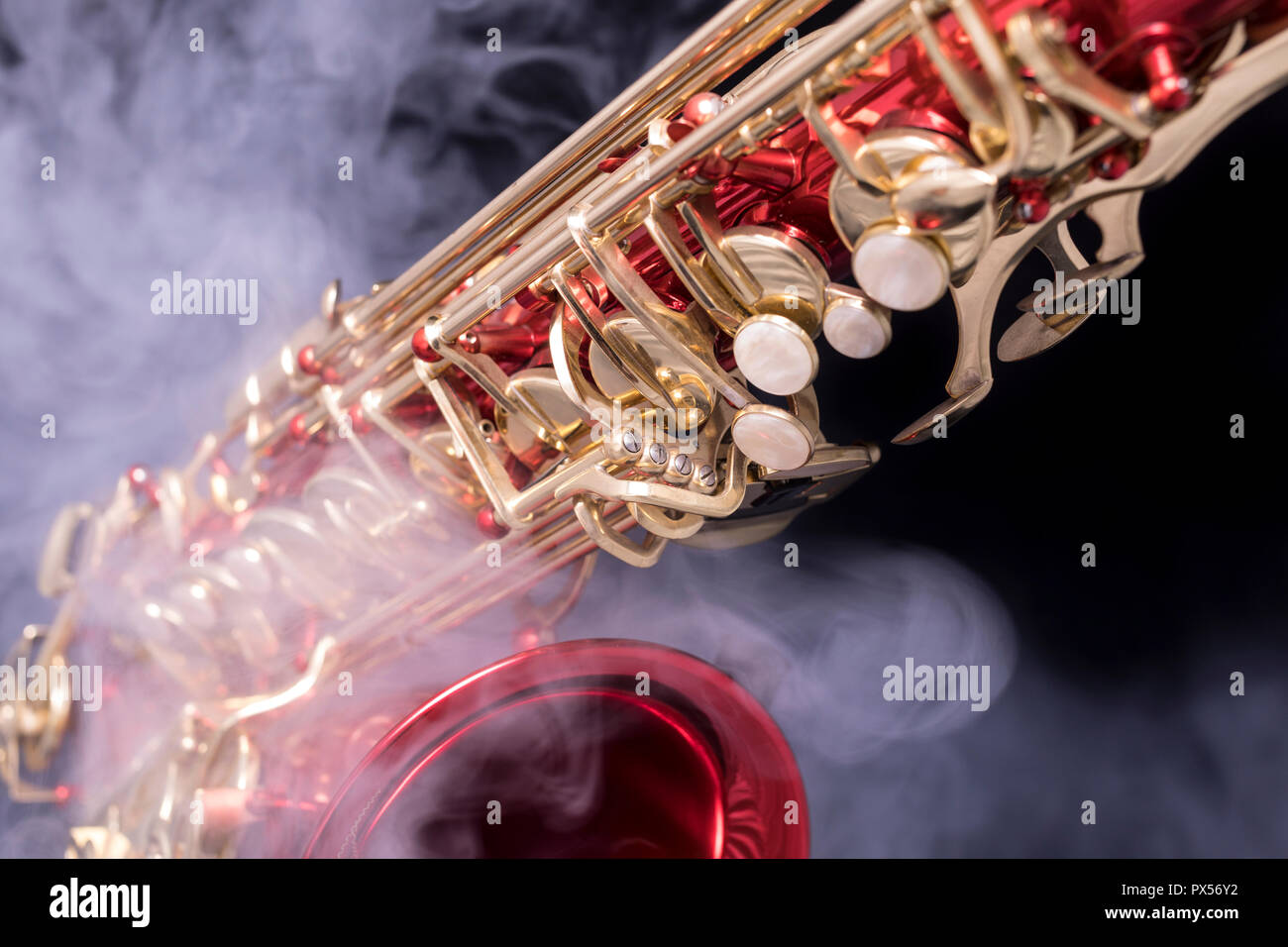 A red lacquered saxophone with gold plated keys in smoke on a black ...