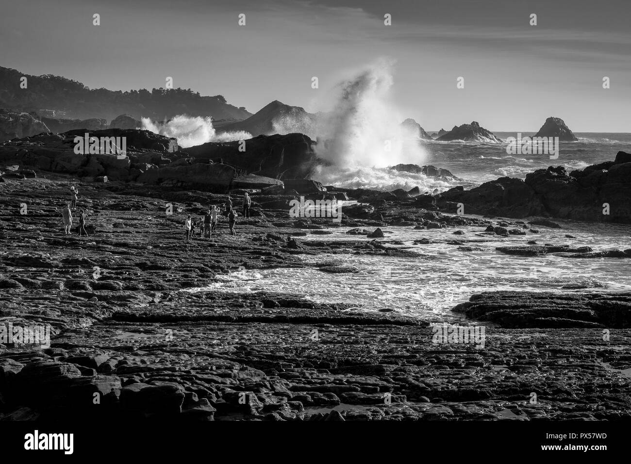 People walking among the rockpools with surf breaking over rocks behind ...