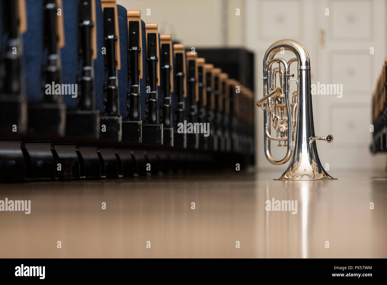 A euphonium standing on its bell on the floor amongst rows of chairs ...