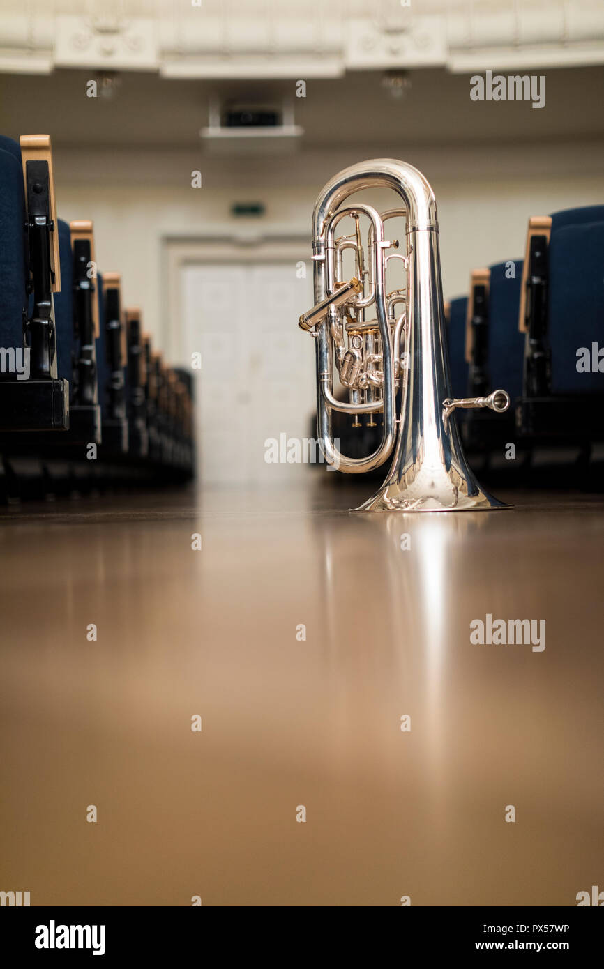 A euphonium standing on its bell on the floor amongst rows of chairs ...