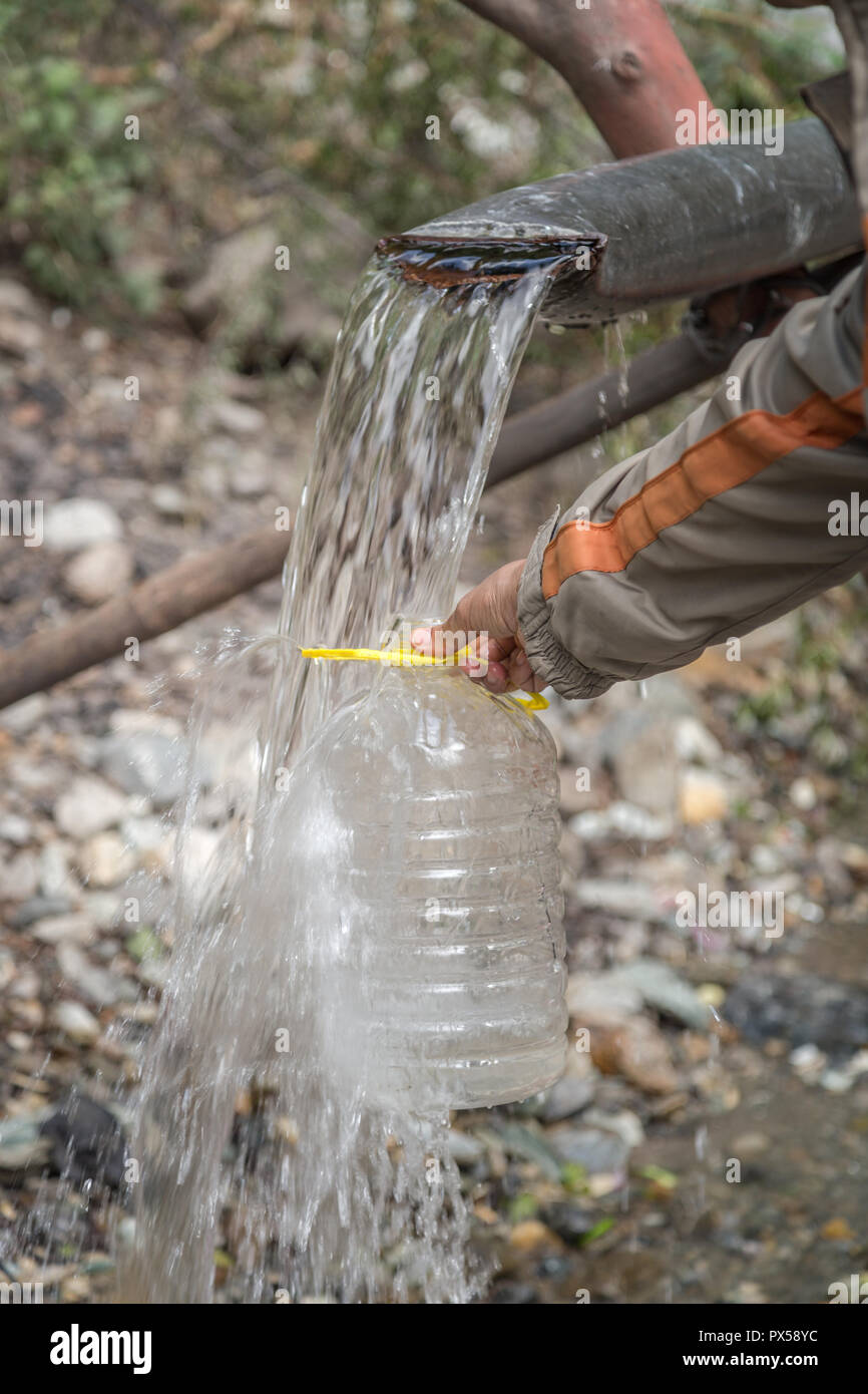Man filling his plastic bottle from Man made fountain from old pipe in ...
