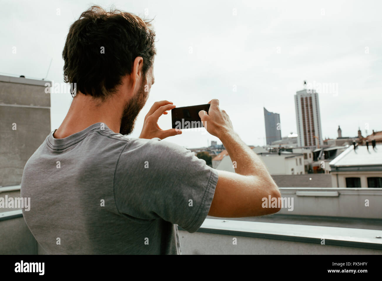 close-up photo of rear view of young man photographing a city skyline ...