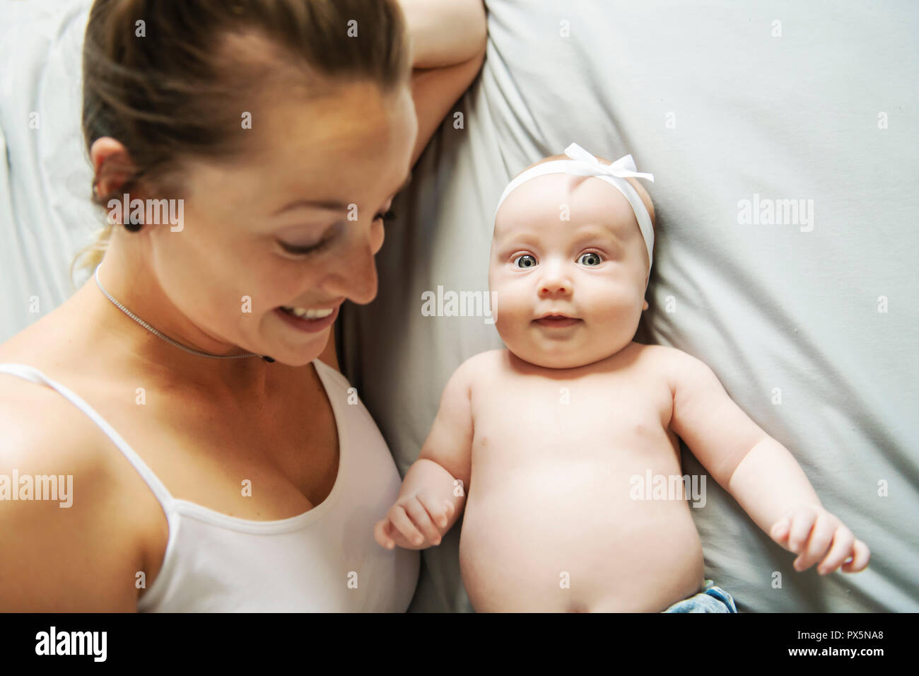 Portrait of a beautiful mother with her 2 month old baby in the bedroom ...