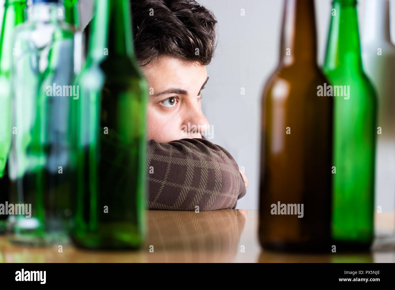 Sad young man behind green and brown glass bottles. Fighting alcohol ...