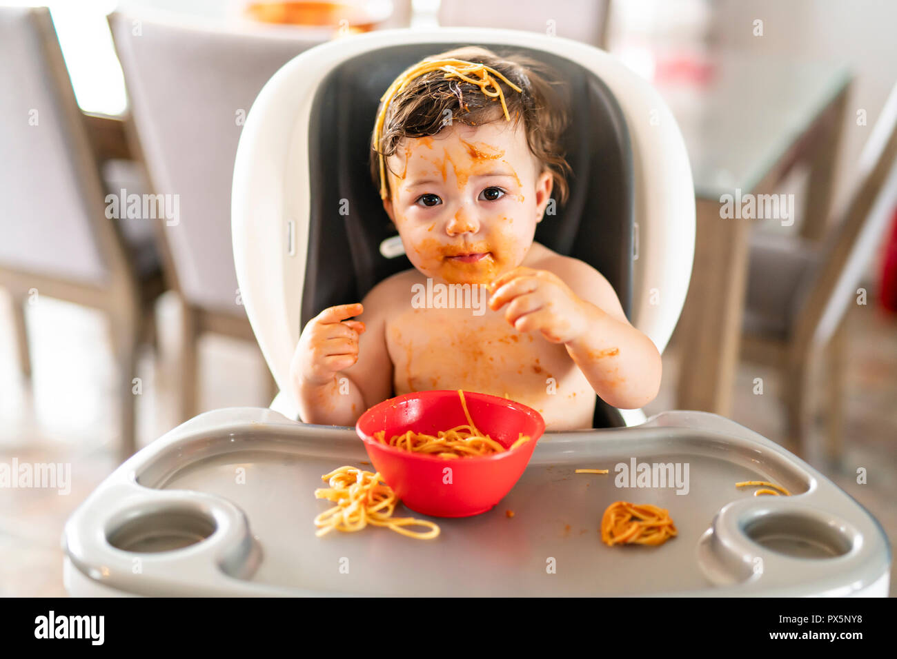 A child girl, eating spaghetti for lunch and making a mess at home in ...