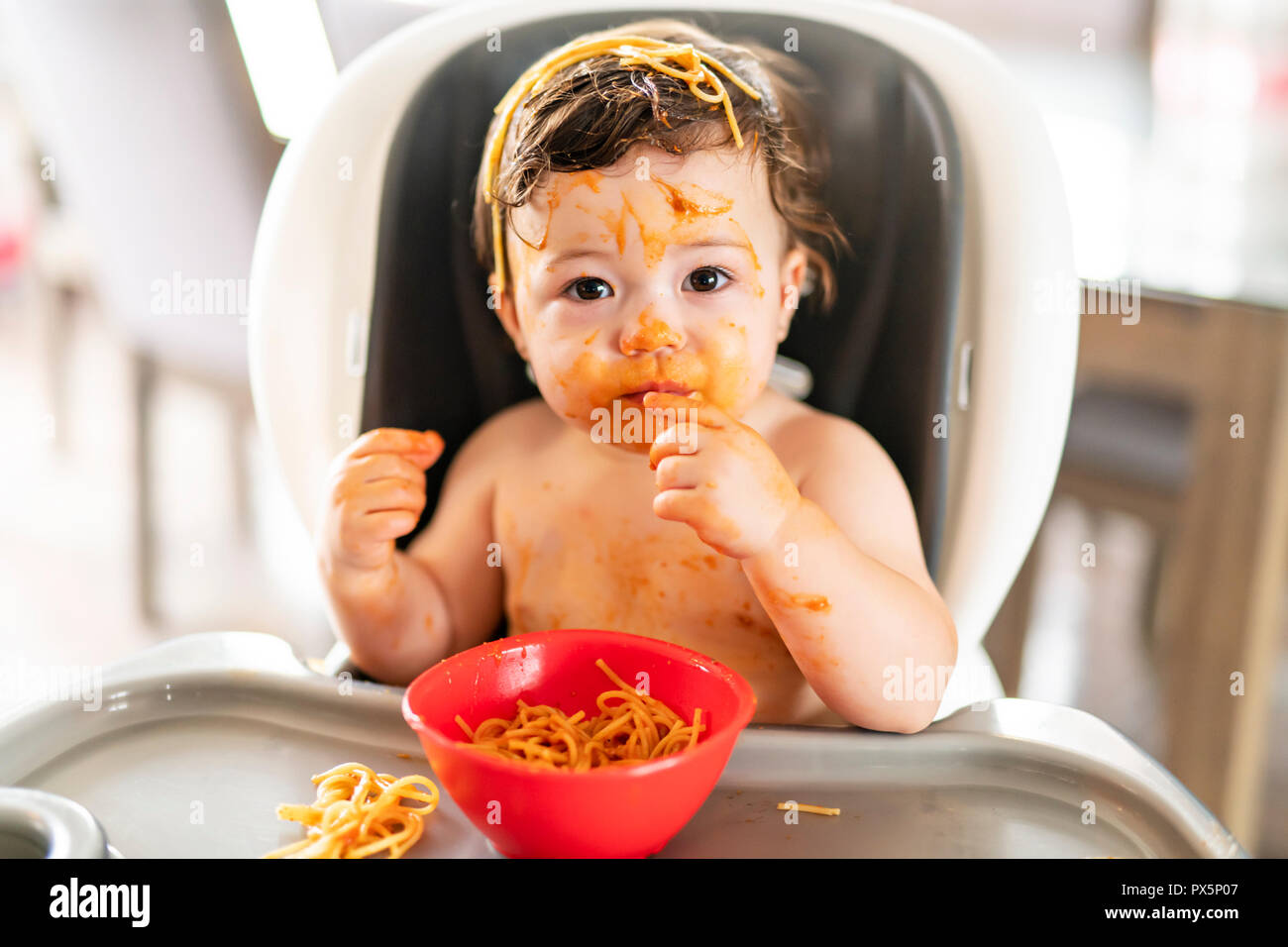 A child girl, eating spaghetti for lunch and making a mess at home in ...