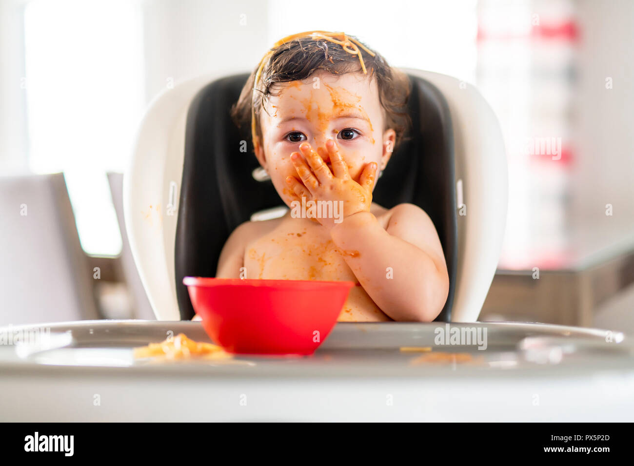 A child girl, eating spaghetti for lunch and making a mess at home in ...