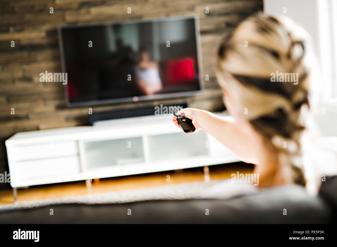A Young woman watching television sitting on the sofa at home. Back ...