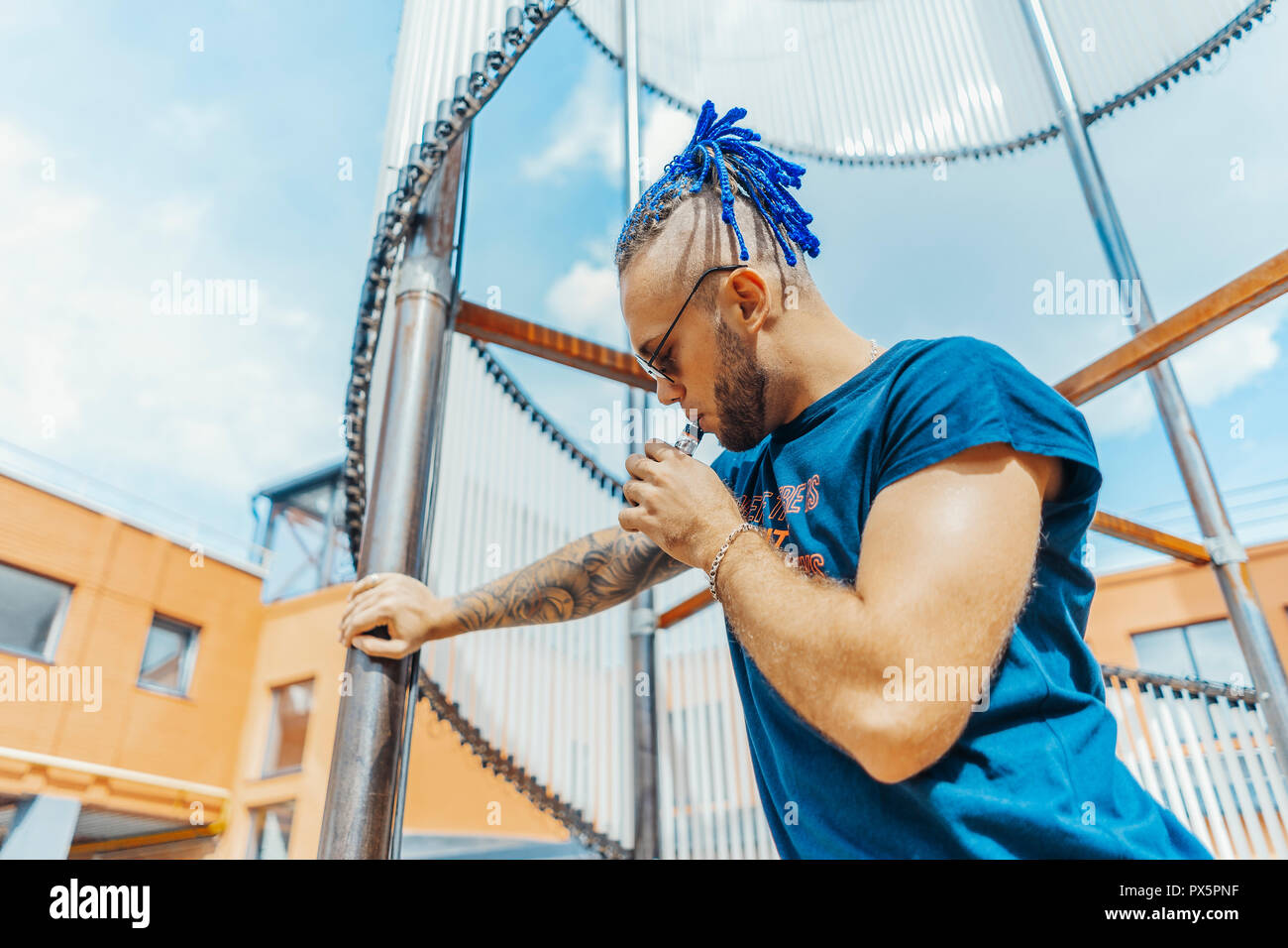Portrait of young vaping man with dreadlocks at art object background ...