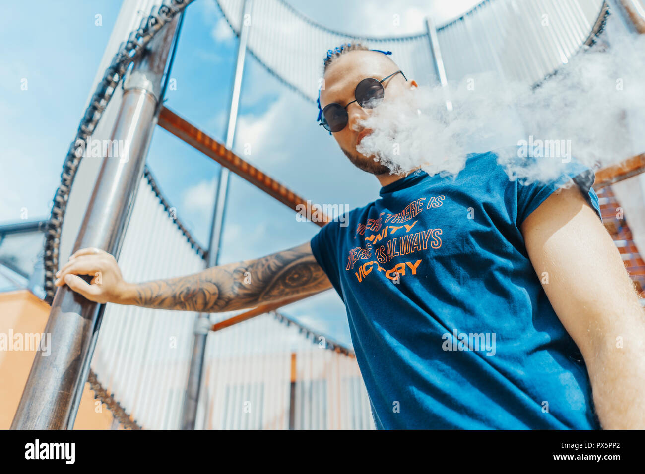 Portrait of young vaping man with dreadlocks at art object background ...