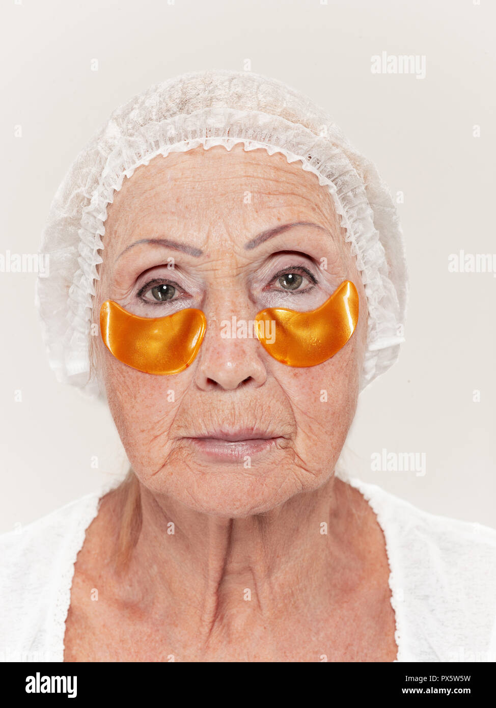 Senior woman isolated on white wall looking at camera making masks ...