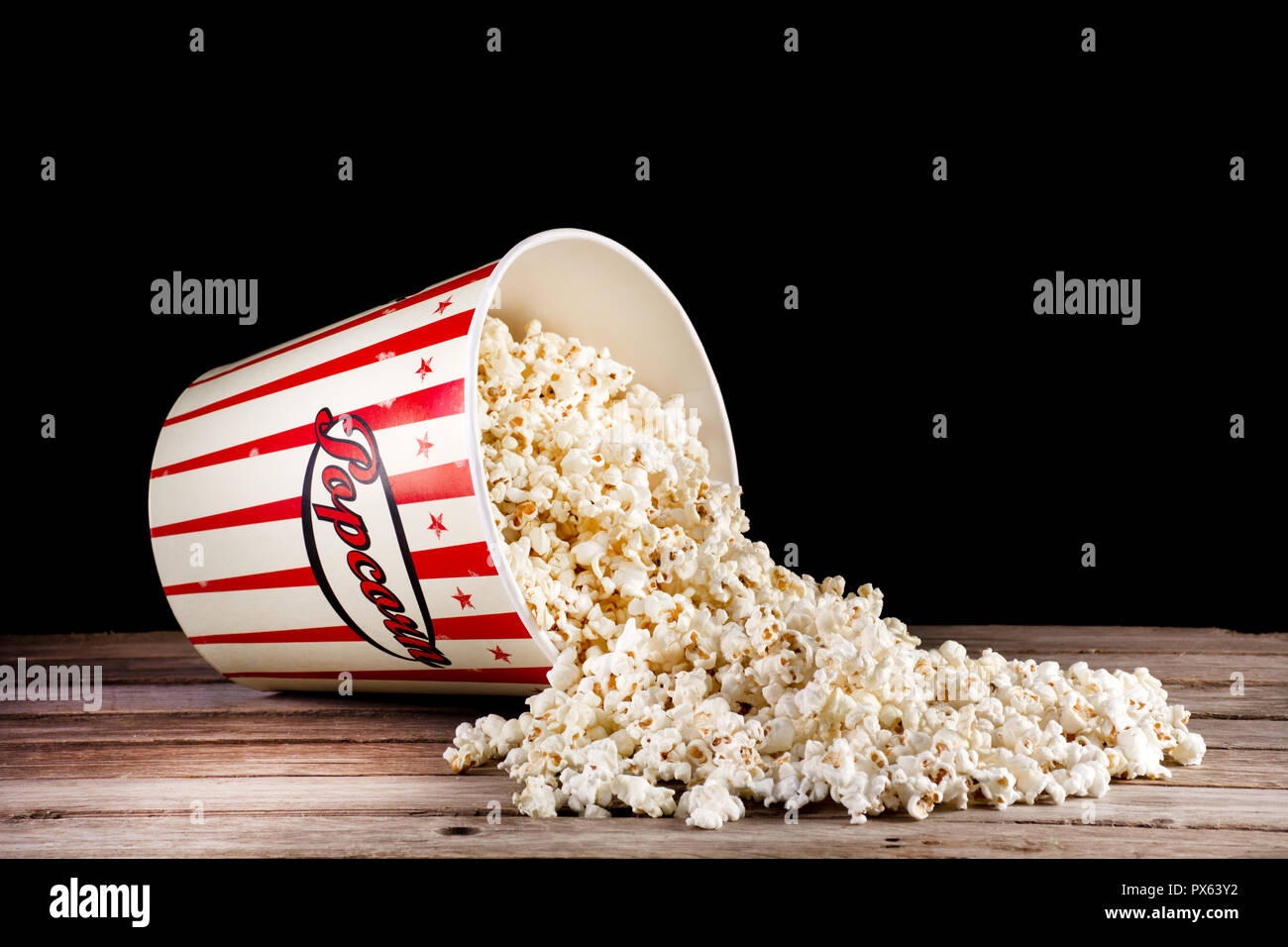 Spilled box with popcorn on retro wooden desk and black background ...