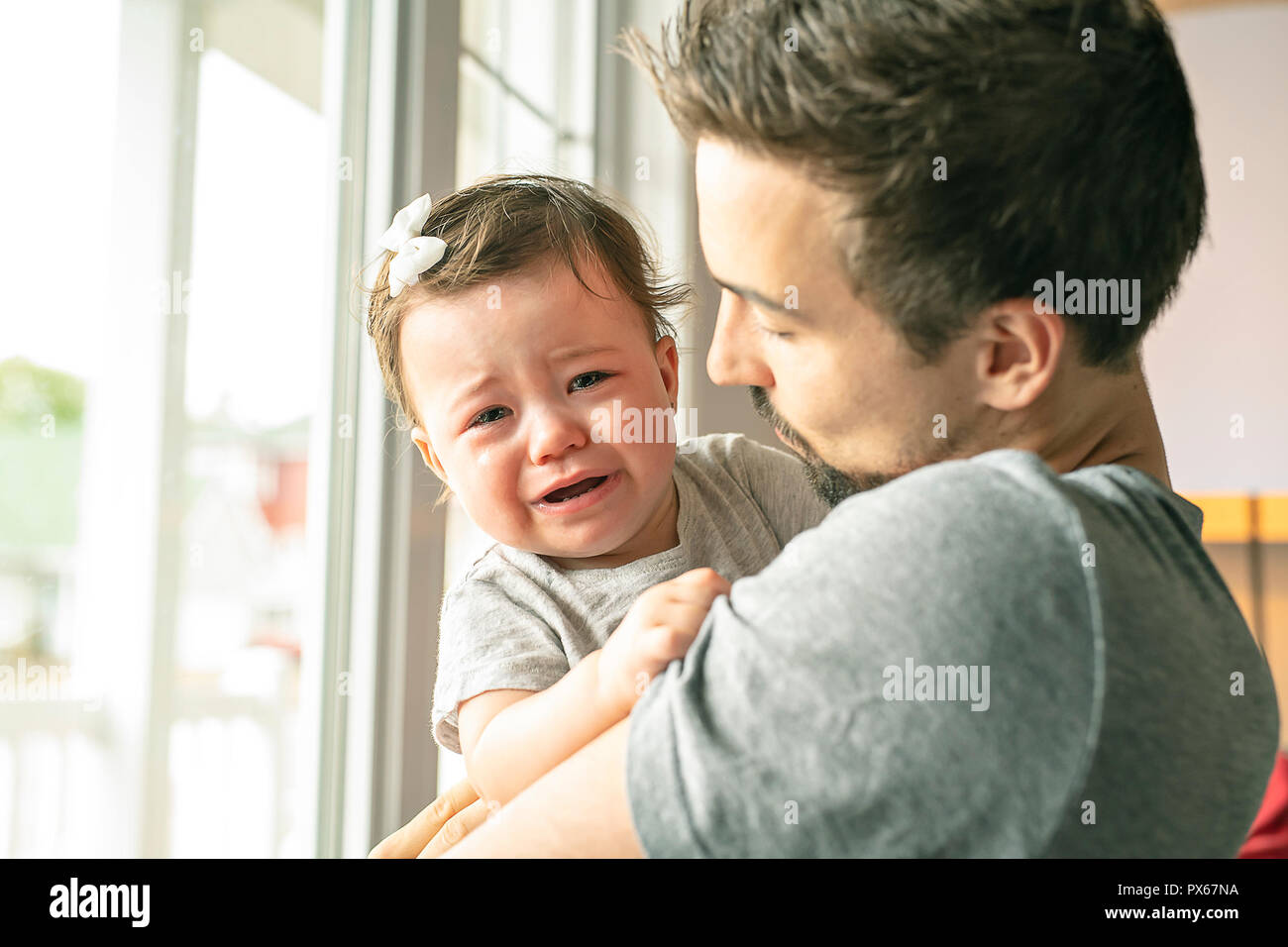 A Father holding little girl close to the window, unhappy girl cry ...