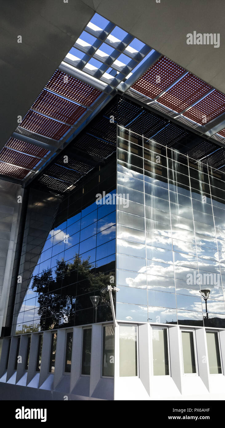 Vertical building with glass windows where clouds and trees reflect the ...