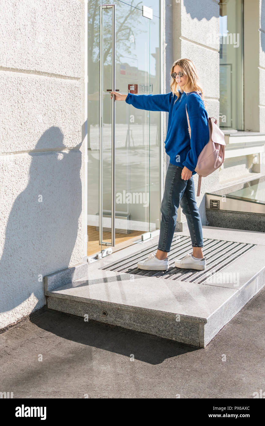 woman with a bag on her shoulder opens the large glass door of the ...