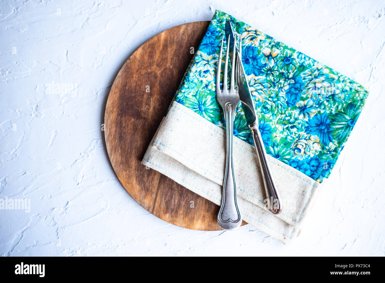 Rustic table setting with bright blue floral napkin on white table with ...