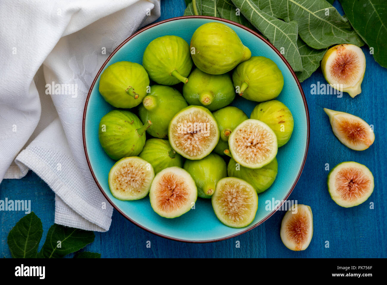 Whole and cut green figs, with fig leaves. Foreground. On colorful ...