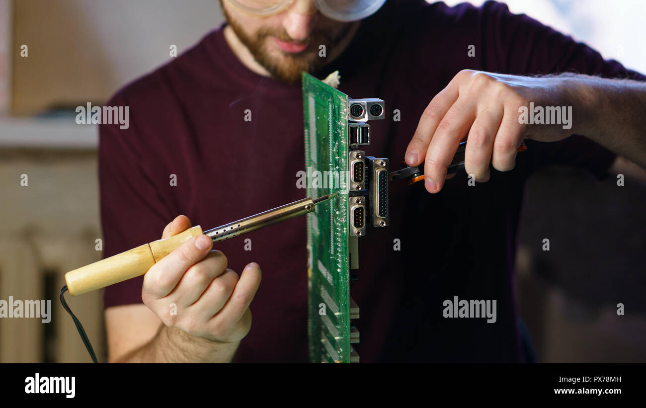 Repair motherboard. Man soldering a soldering iron contacts the details ...