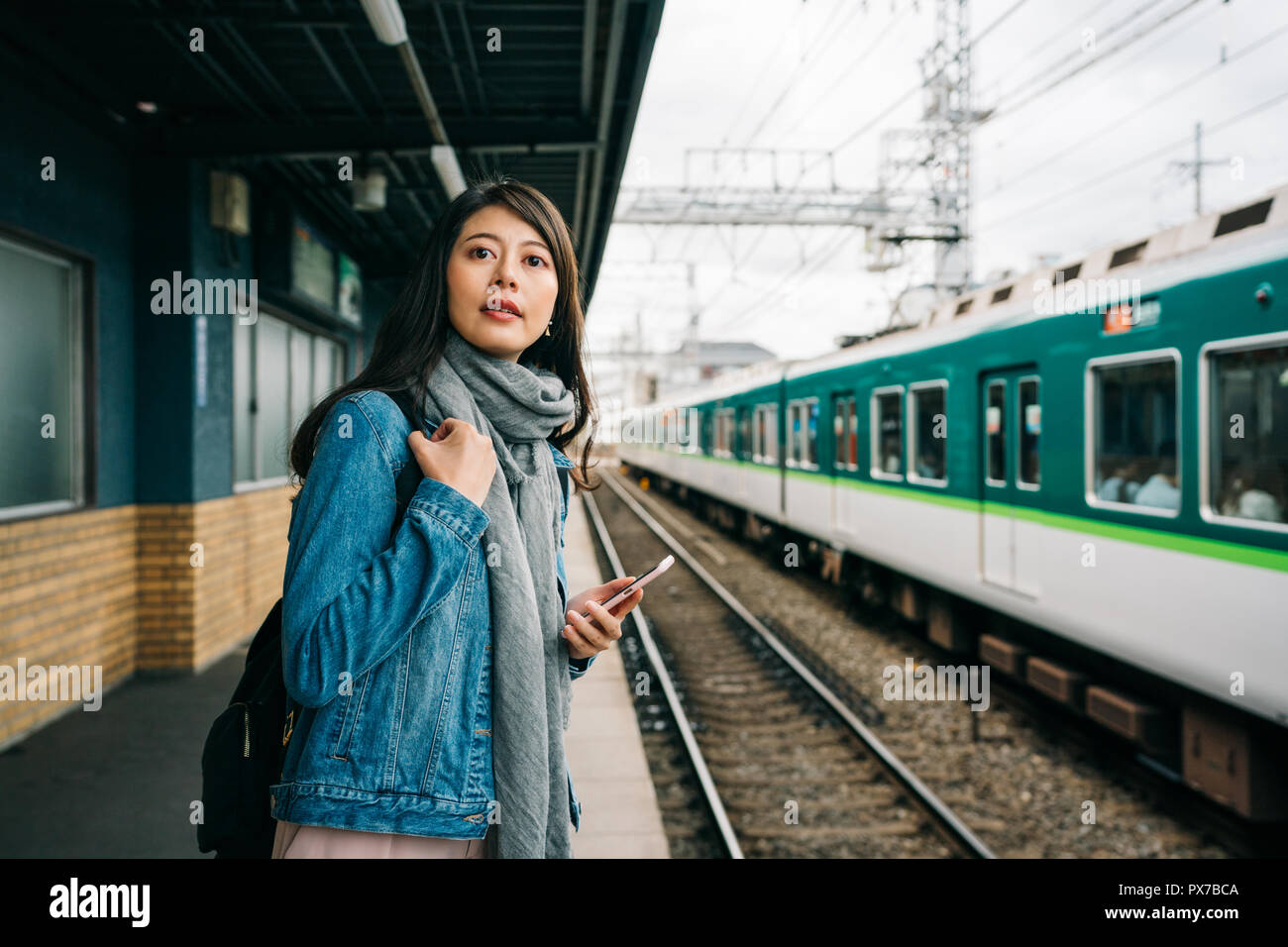 elegant female traveler standing on the station and waiting the train ...