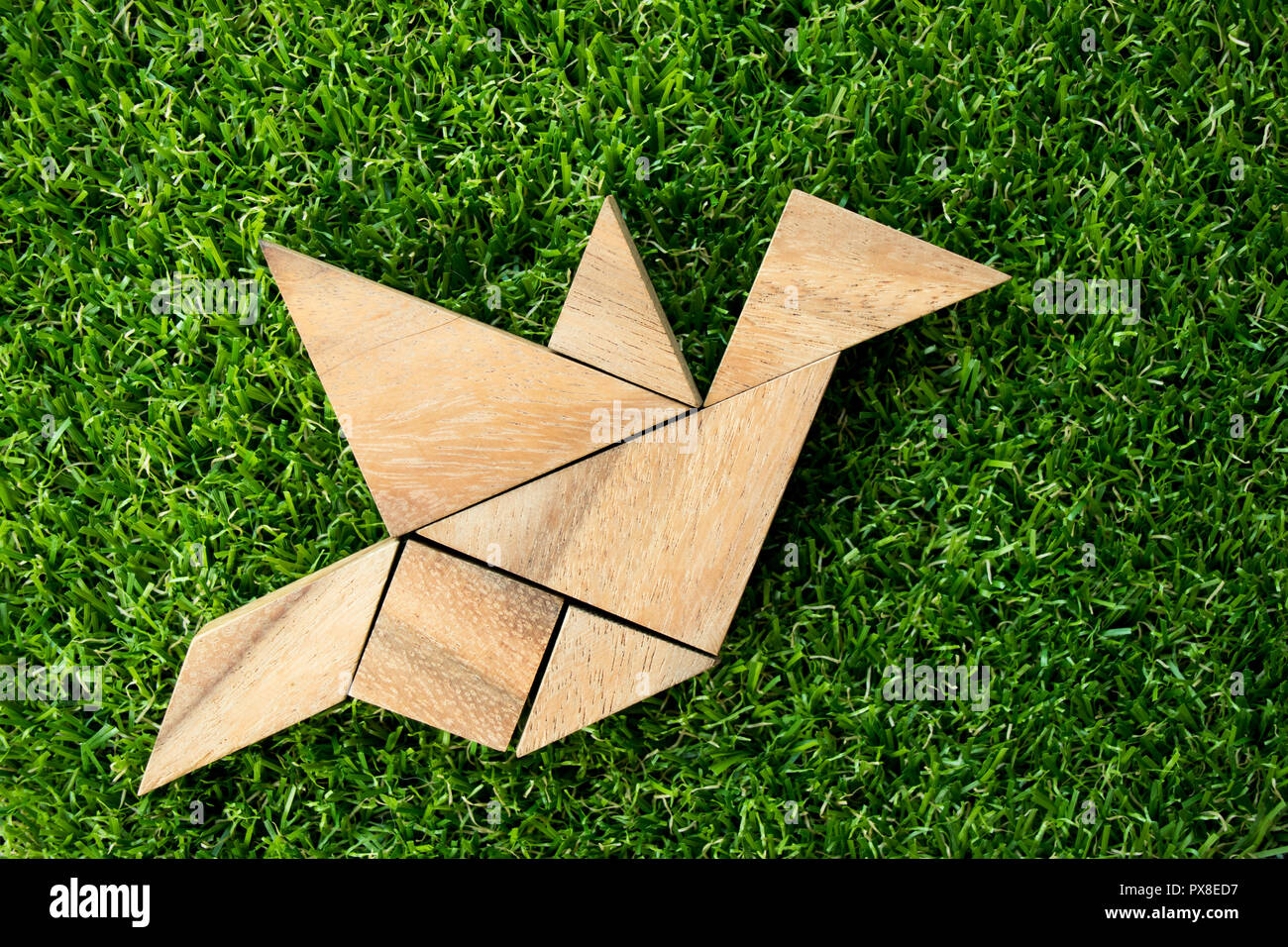 Wooden tangram puzzle in flying bird shape on artificial green grass ...