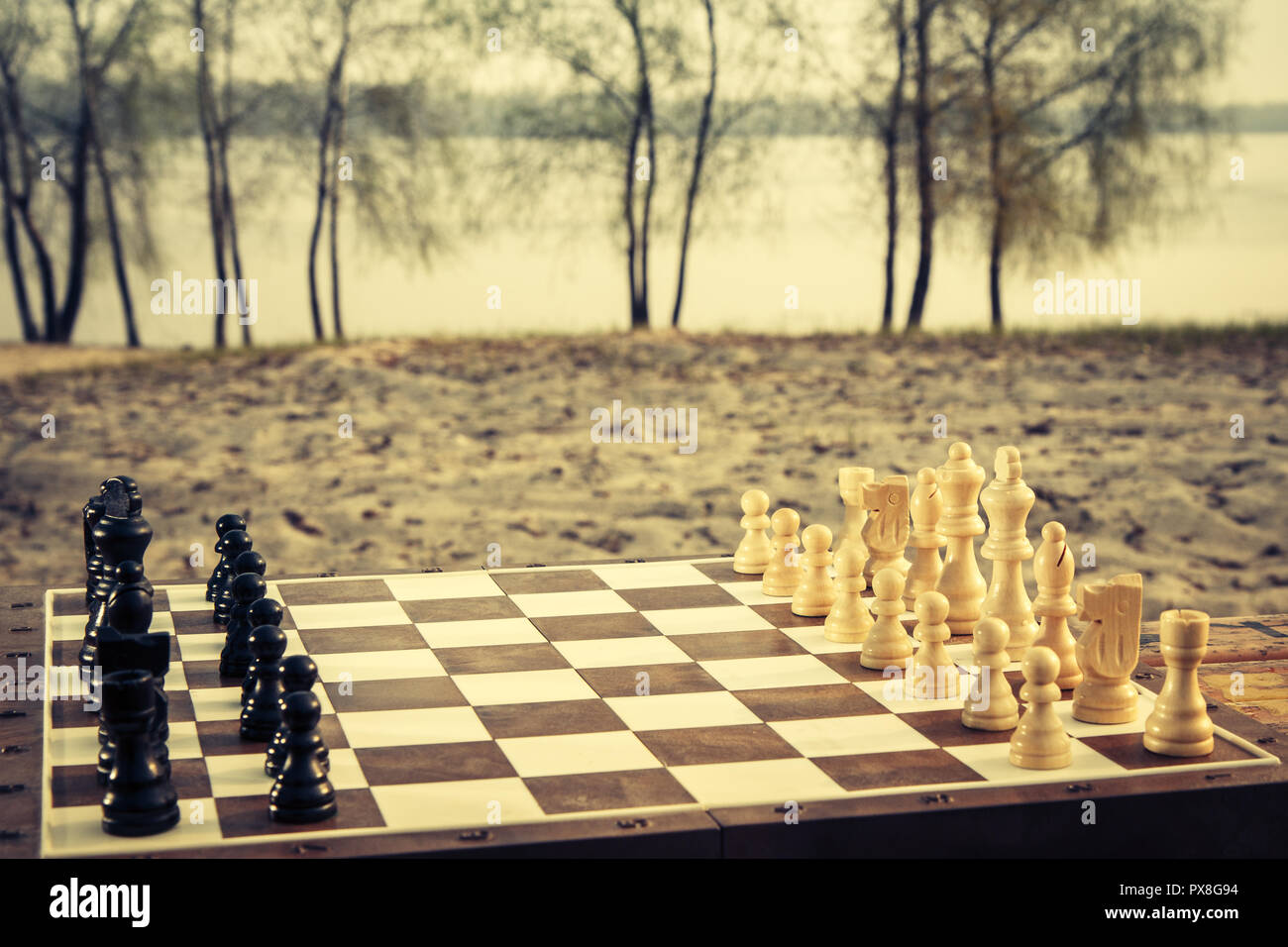 Chess board with chess pieces on wooden bench with river on the ...