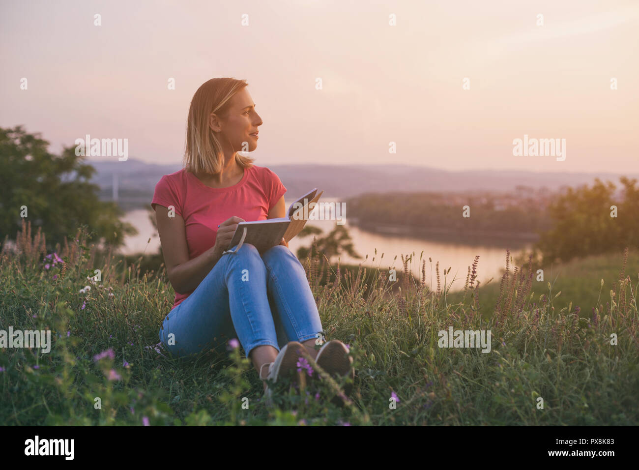 Beautiful woman enjoys writing outdoor with a cityscape and river view ...