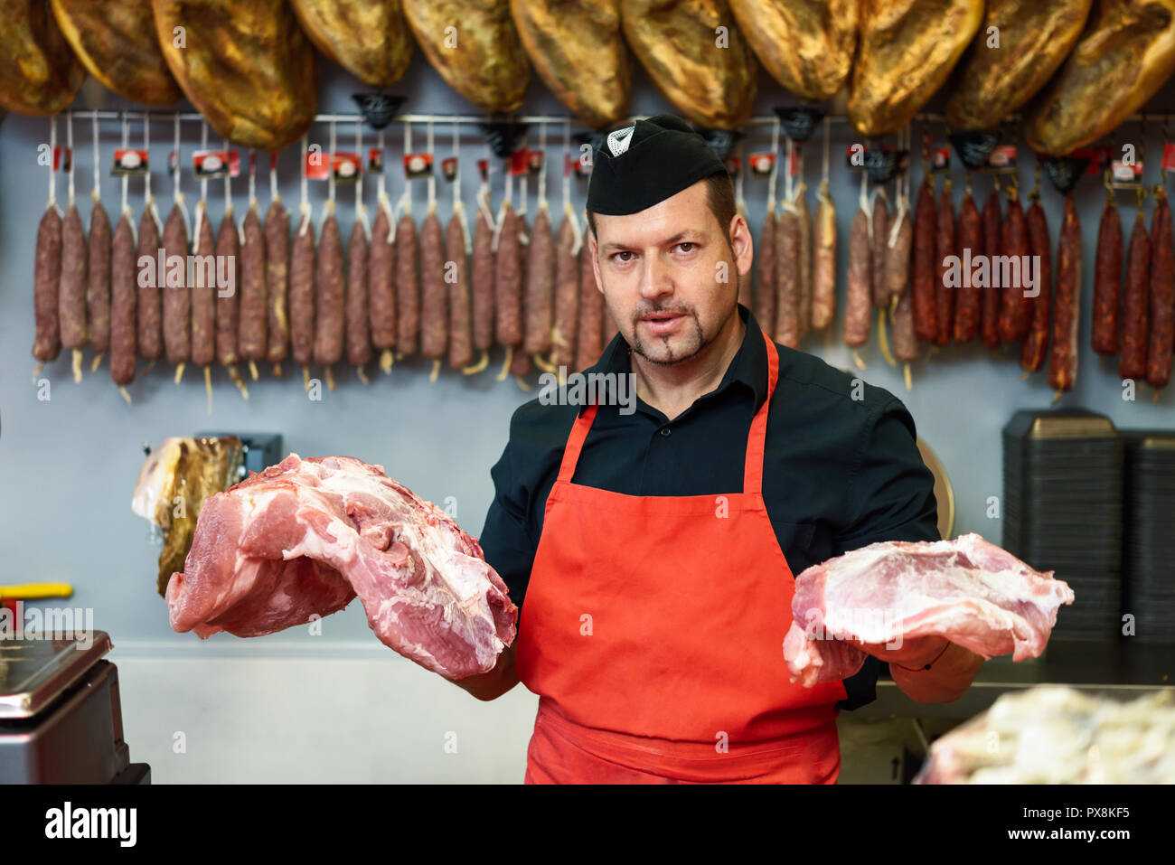 Portrait of a handsome butcher holding meat standing in a butcher shop ...