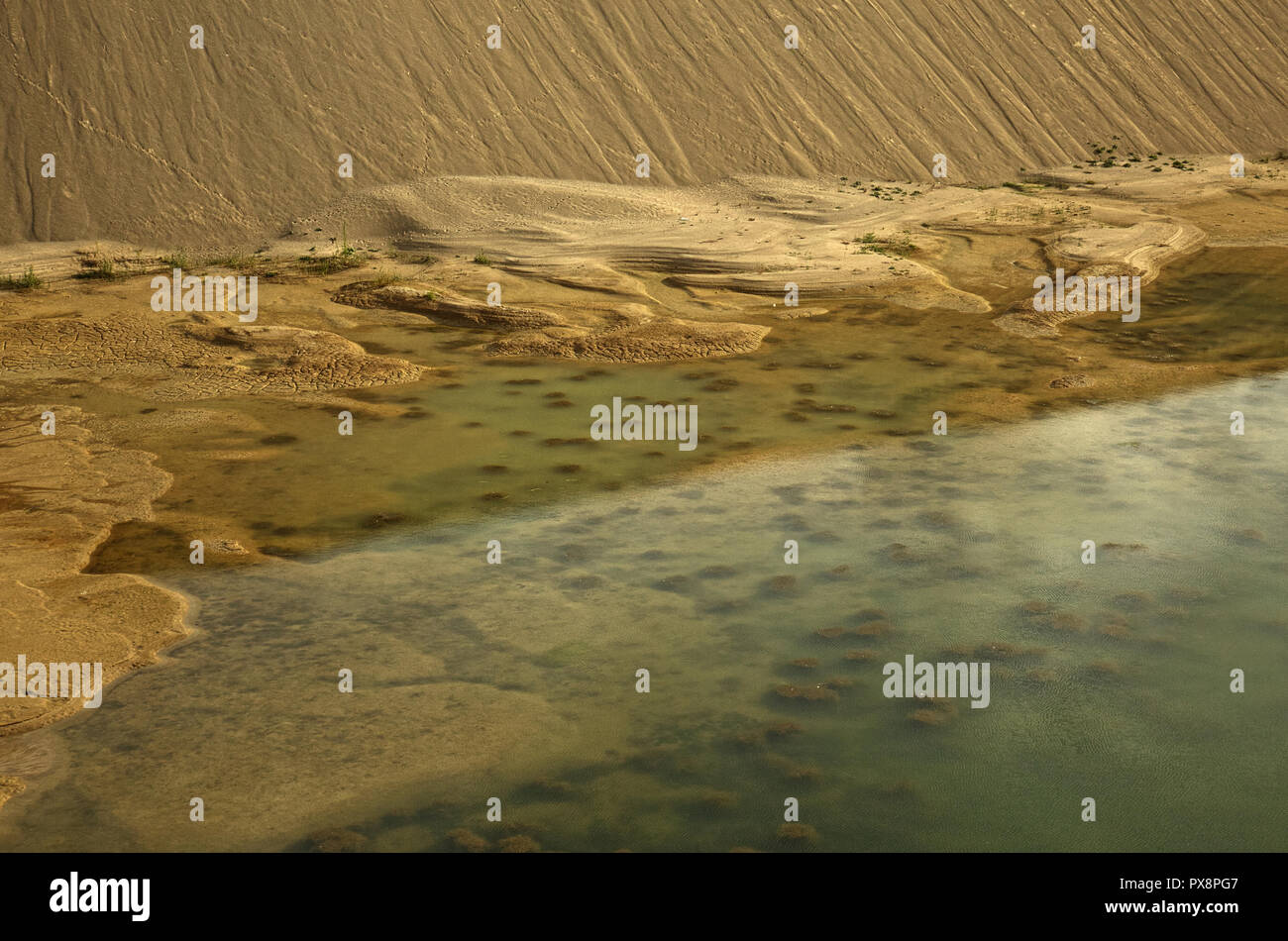 Pond with visible bottom, stones in the water and heaps of sand with a ...
